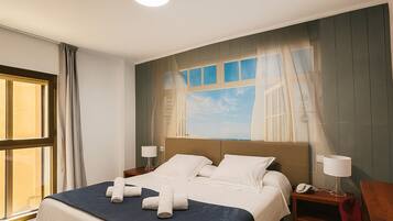Quarto de hotel com cama, duas mesas de cabeceira, janela com cortinas e vista do céu.