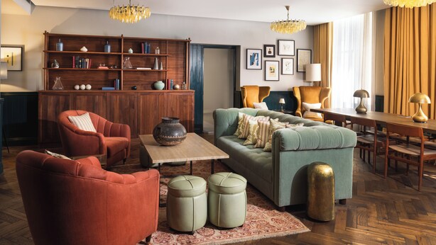Uma sala de estar aconchegante com uma estante de madeira, uma poltrona vermelha, um sofá verde e uma mesa de jantar com cadeiras.