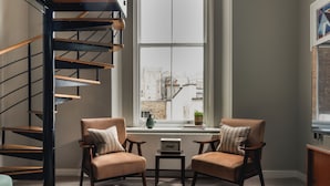Uma sala de estar moderna com escada em espiral, dois poltronas, uma mesa pequena e uma grande janela com vista para a cidade.