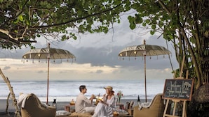 Cenário de praia com duas cadeiras de praia sob guarda-sóis, uma lousa e vista para o mar.