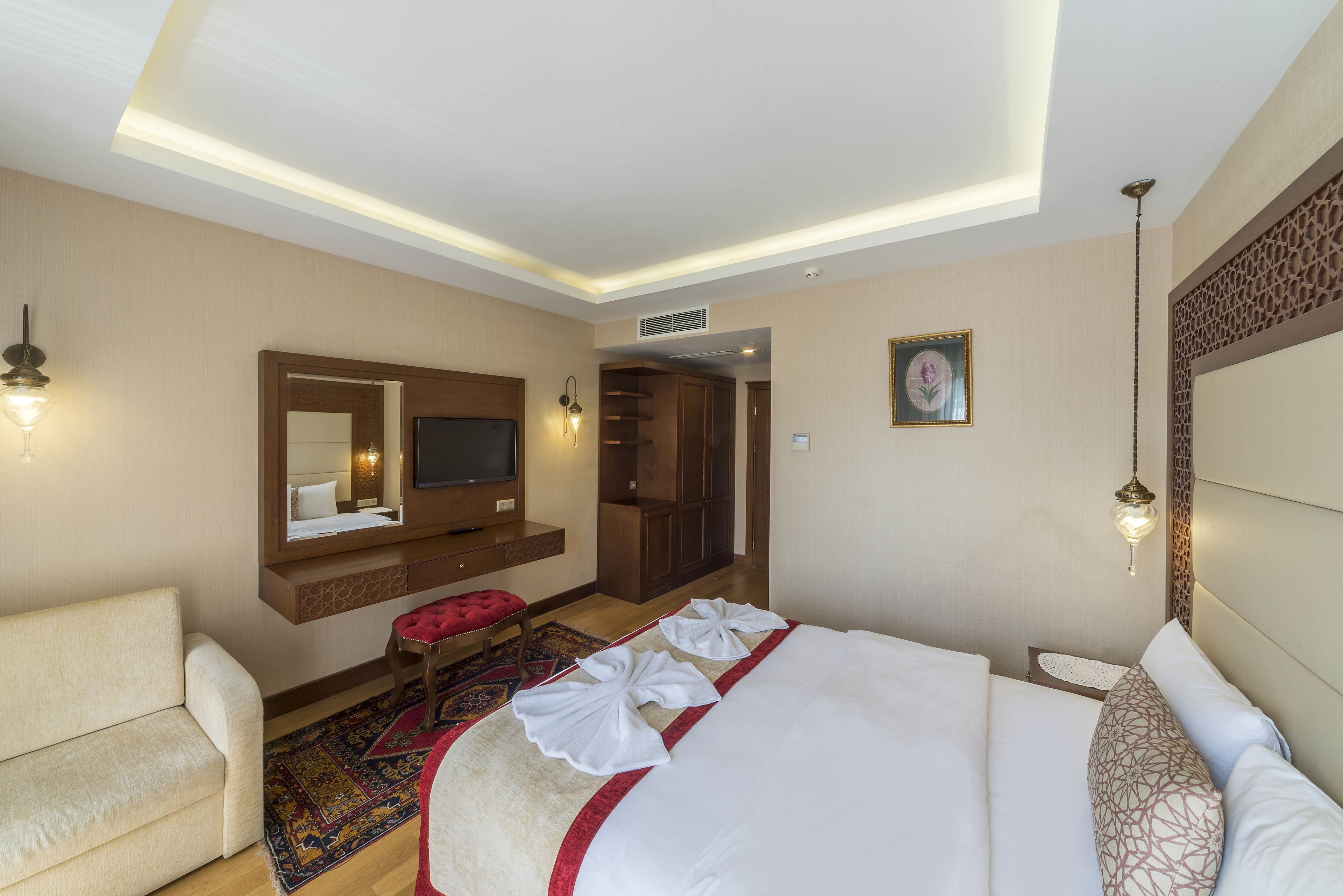 Quarto de hotel com cama, sofá, escrivaninha, espelho, televisão e armário.