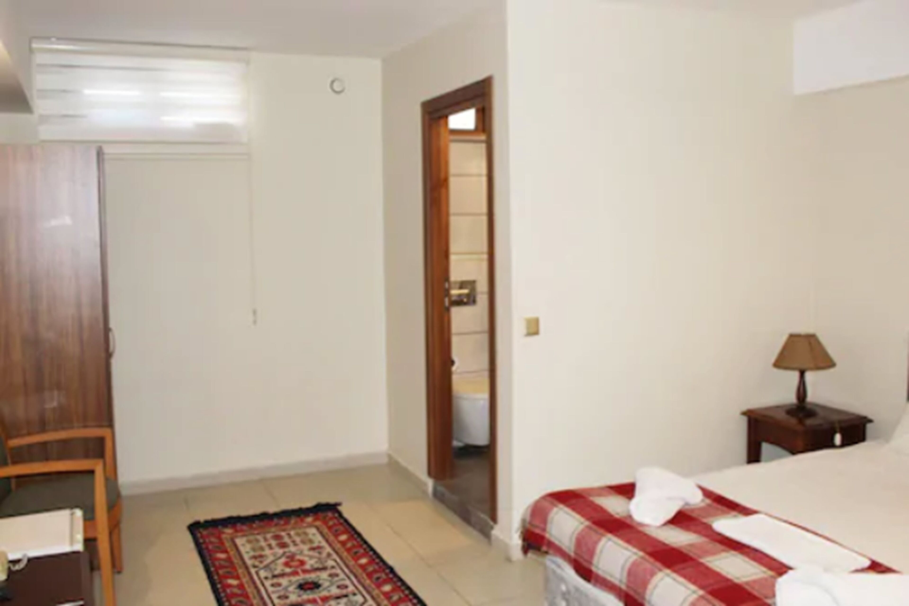 Quarto com cama, mesa de cabeceira, abajur, guarda-roupa de madeira e tapete estampado.