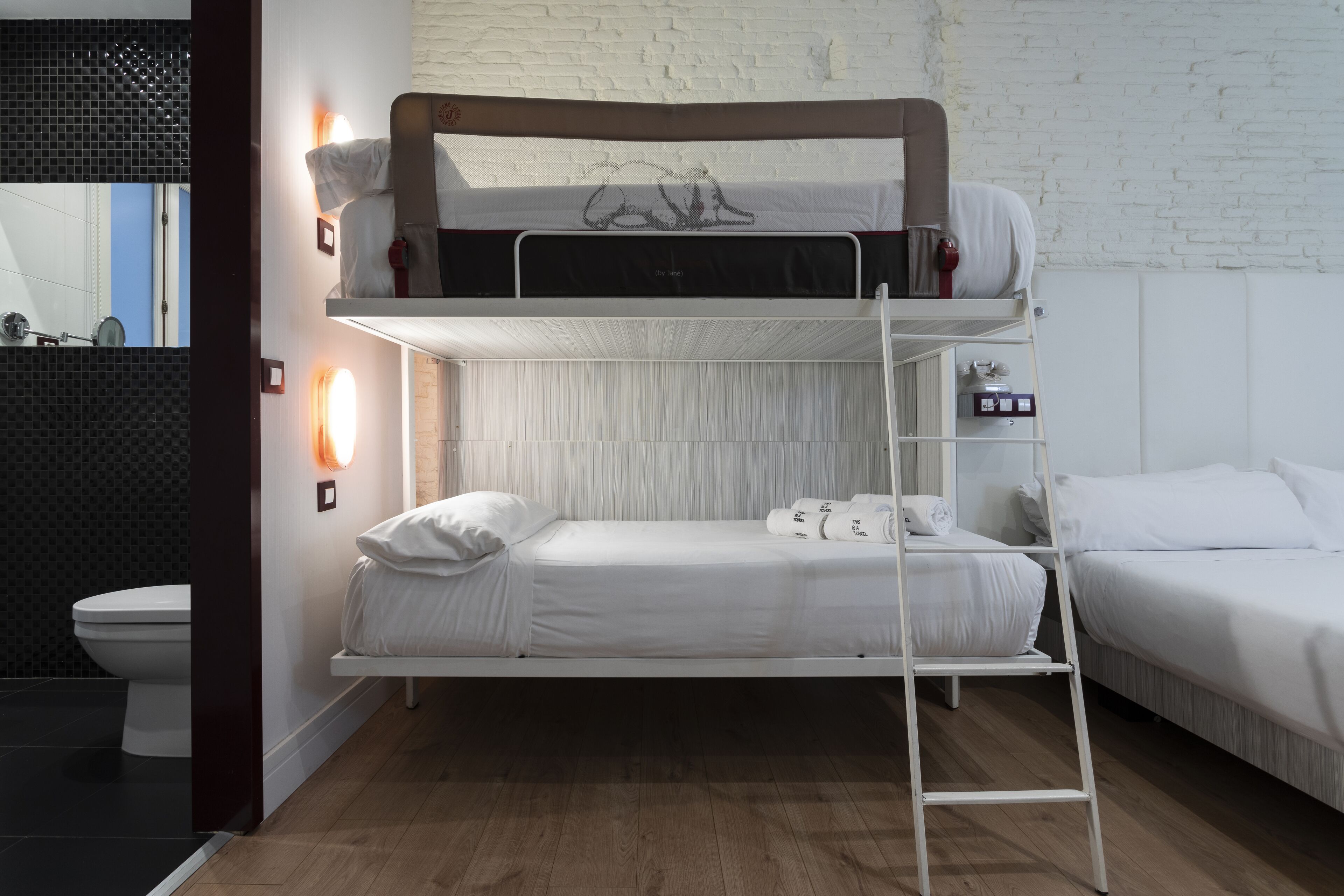 Quarto com beliche, cabeceira branca, escada de madeira e vaso sanitário branco.