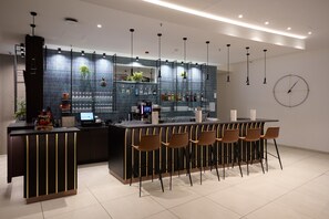 Uma área de bar moderna com balcão, banquetas e um relógio na parede.