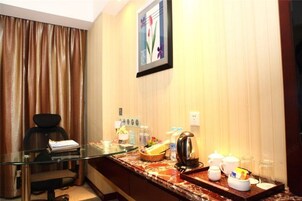 Quarto de hotel com secretária de vidro, uma cadeira, cama, quadro na parede e minibar.