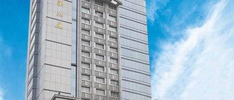 Hotel com vários andares, entrada imponente e estacionamento em frente.