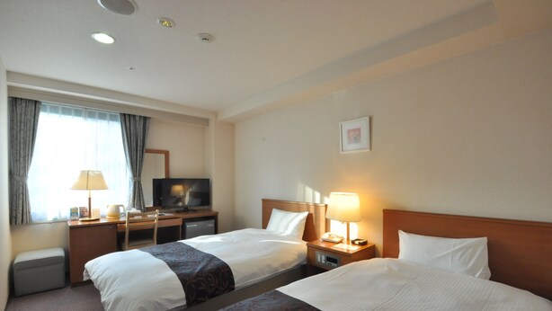 Quarto de hotel com duas camas, uma escrivaninha, televisão e janela com cortinas.