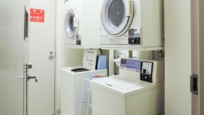 Uma área de lavanderia com duas máquinas de lavar e uma secadora, uma escada de metal e uma porta com um aviso.