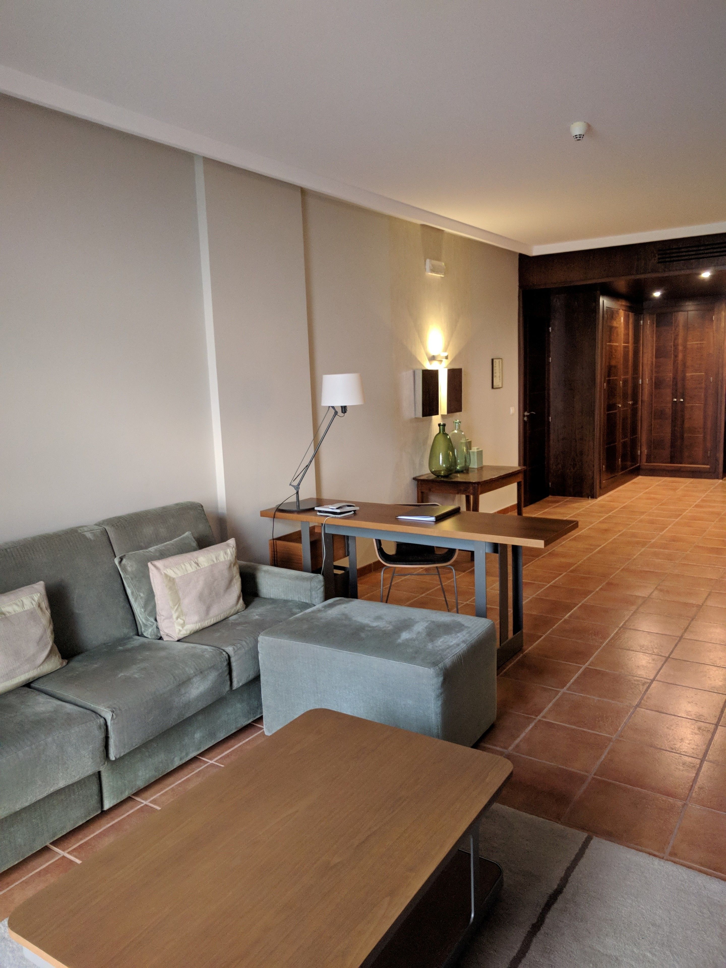 Uma sala de estar moderna com um sofá cinza, uma mesa de centro de madeira e uma escrivaninha com uma luminária.