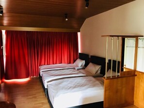 Quarto de hotel com duas camas, piso de madeira, cortina vermelha e cabeceira de madeira.
