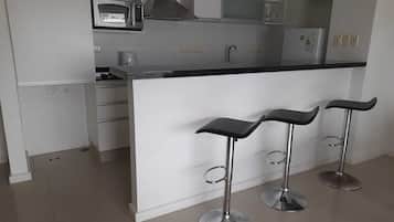 Uma cozinha moderna com armários brancos, bancada preta e dois banquetas de aço inoxidável.