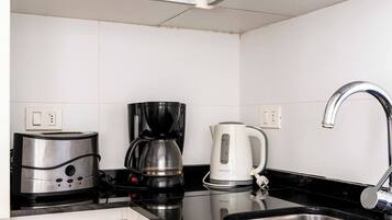 Uma cozinha moderna com uma torradeira de aço inoxidável, uma cafeteira preta e uma chaleira elétrica branca.