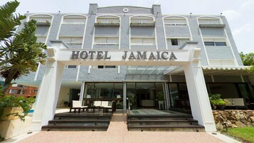 A entrada do Hotel Jamaica, com fachada moderna, grandes portas de vidro e uma escadaria de pedra que leva à entrada.