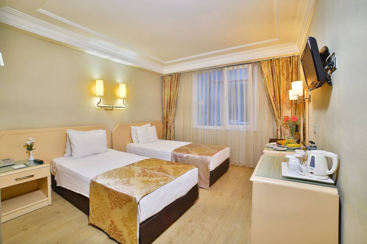 Quarto de hotel com duas camas, uma escrivaninha com chaleira e televisão na parede.