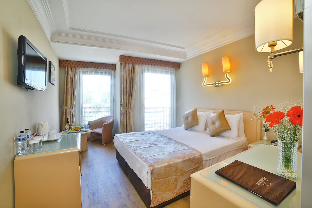 Quarto de hotel com cama, mesa de cabeceira, televisão e escrivaninha com cadeira.