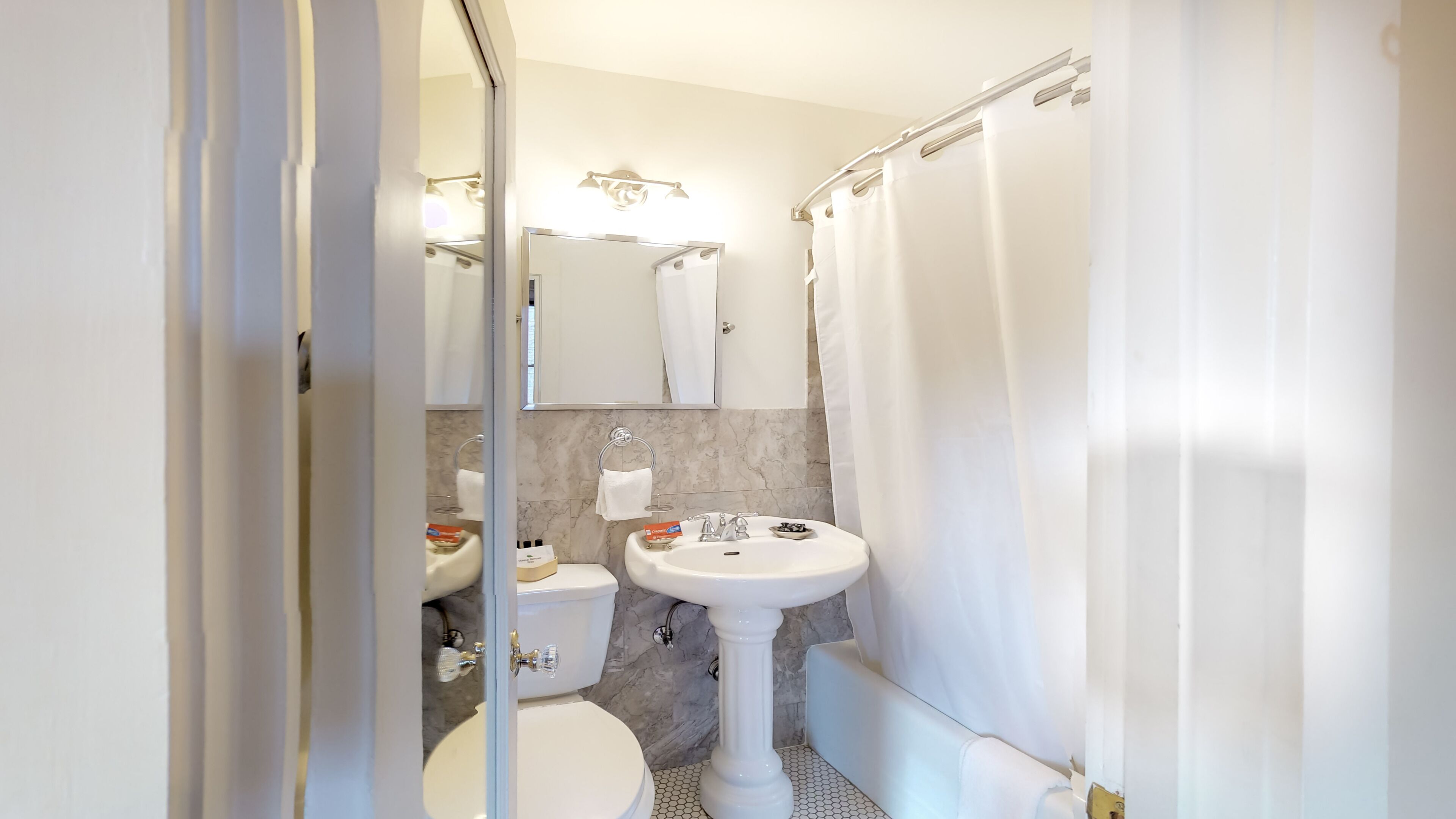 Casa de banho com lavatório branco, sanita e banheira. Há um porta-toalhas acima do lavatório e uma cortina de chuveiro.