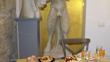 Uma mesa de jantar com diversos itens de café da manhã, uma estátua de um cavalo e uma figura humana, e uma cadeira.