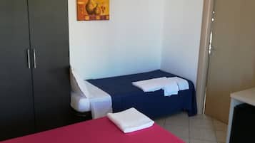 Quarto com uma cama vermelha, uma cama azul e um guarda-roupa. Há um quadro na parede e um ar condicionado sobre as camas.