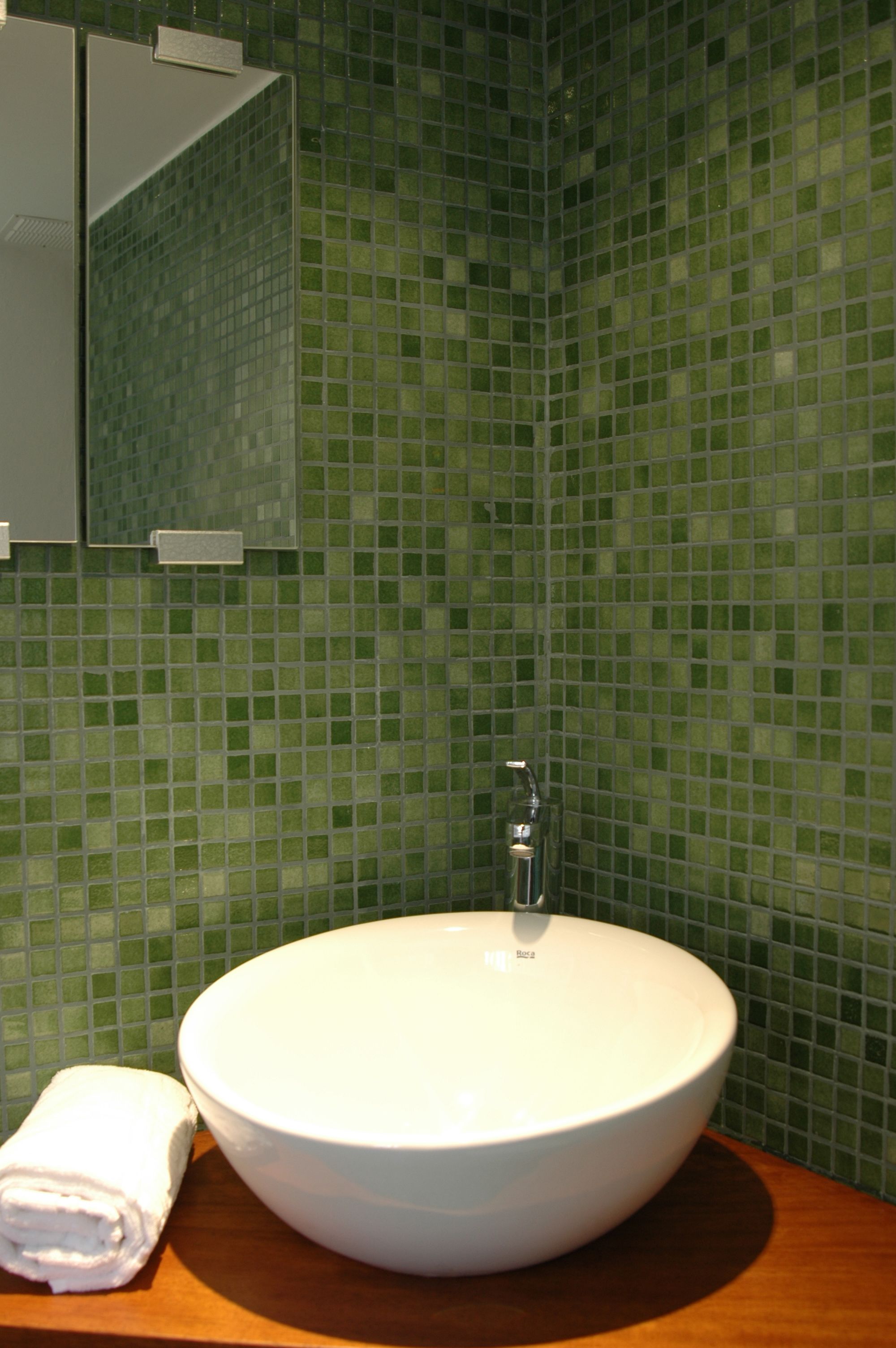Um banheiro com pia branca, espelho e azulejos de mosaico verde.