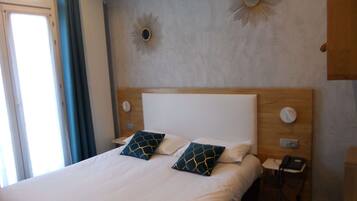 Quarto de hotel com uma cama grande, duas arandelas, uma cabeceira de madeira e um telefone no criado-mudo.