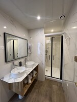 Uma casa de banho moderna com duas pias, um espelho grande e cabine de duche com vidro.