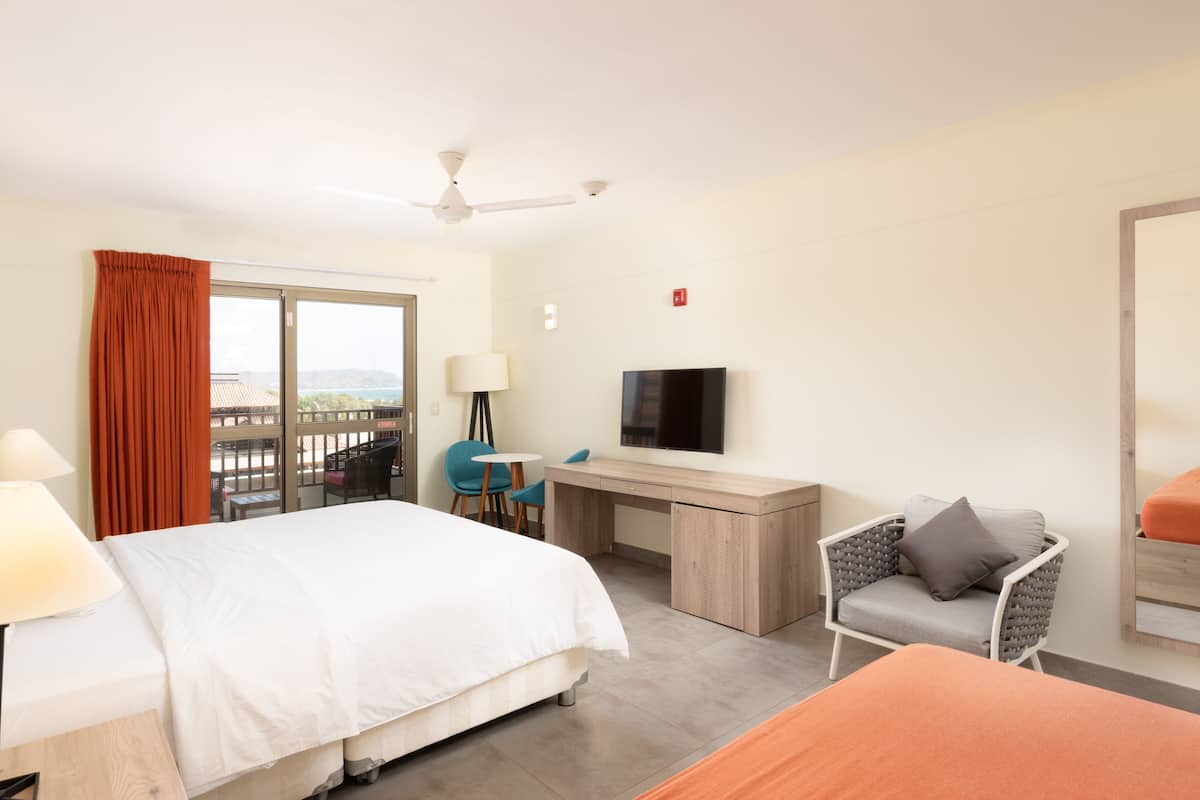 Quarto de hotel com cama, escrivaninha, cadeira, televisão e varanda com vista.