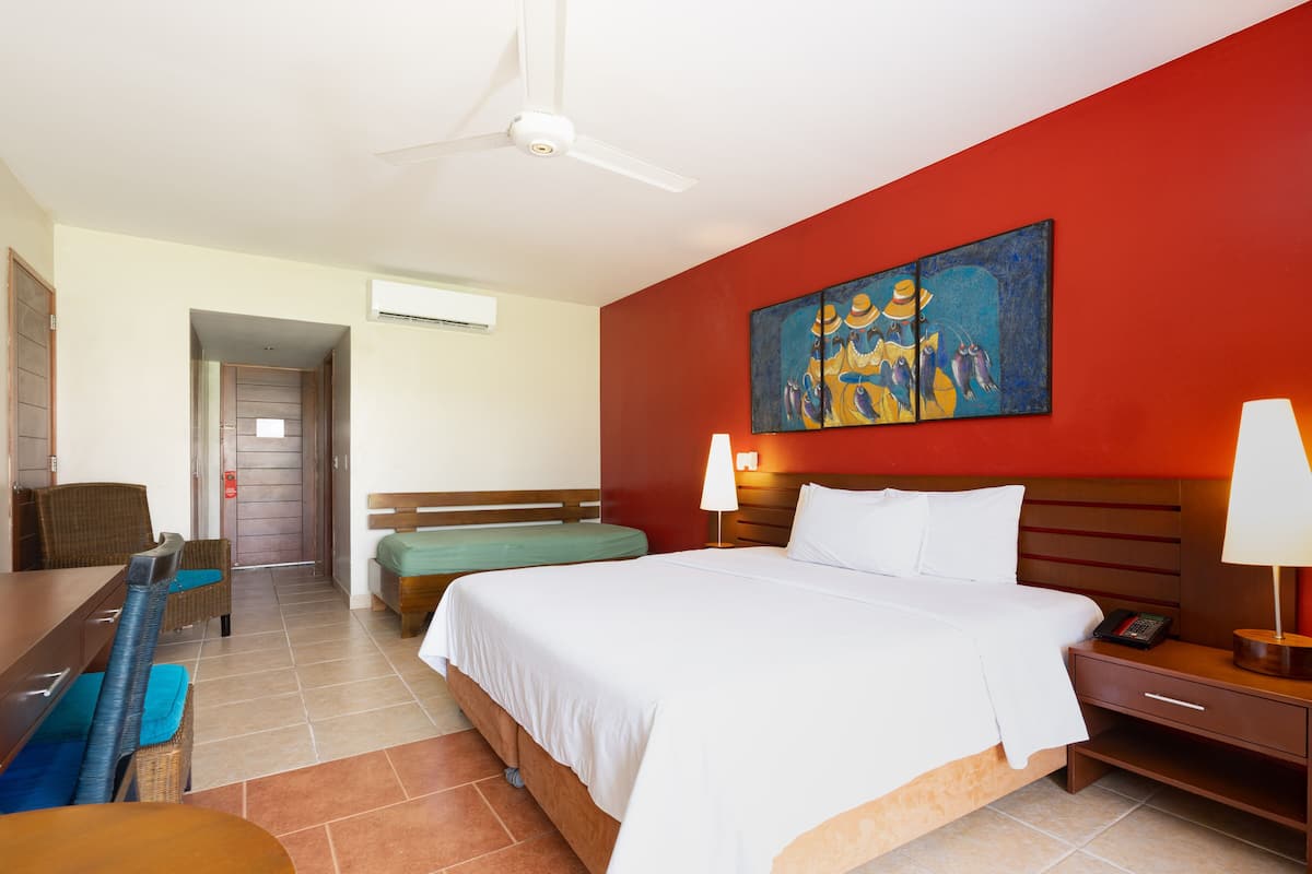 Quarto de hotel com cama, escrivaninha, cadeira, mesa de cabeceira e um quadro na parede.