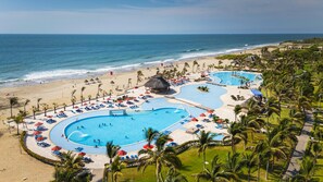 Um resort com várias piscinas, uma praia e palmeiras.