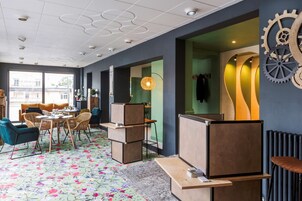 Um interior moderno com carpete floral, uma área de jantar com cadeiras e uma mesa, e uma parede com decoração de engrenagens.