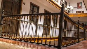 Uma escadaria imponente com grades ornamentadas e um candelabro, que leva a um andar superior com varanda.
