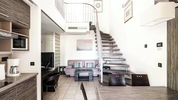 Um espaço de estar moderno com escada, sofá, mesa de jantar e área de cozinha.