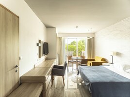 Quarto de hotel moderno com cama, escrivaninha, televisão e varanda com mesa e cadeiras.