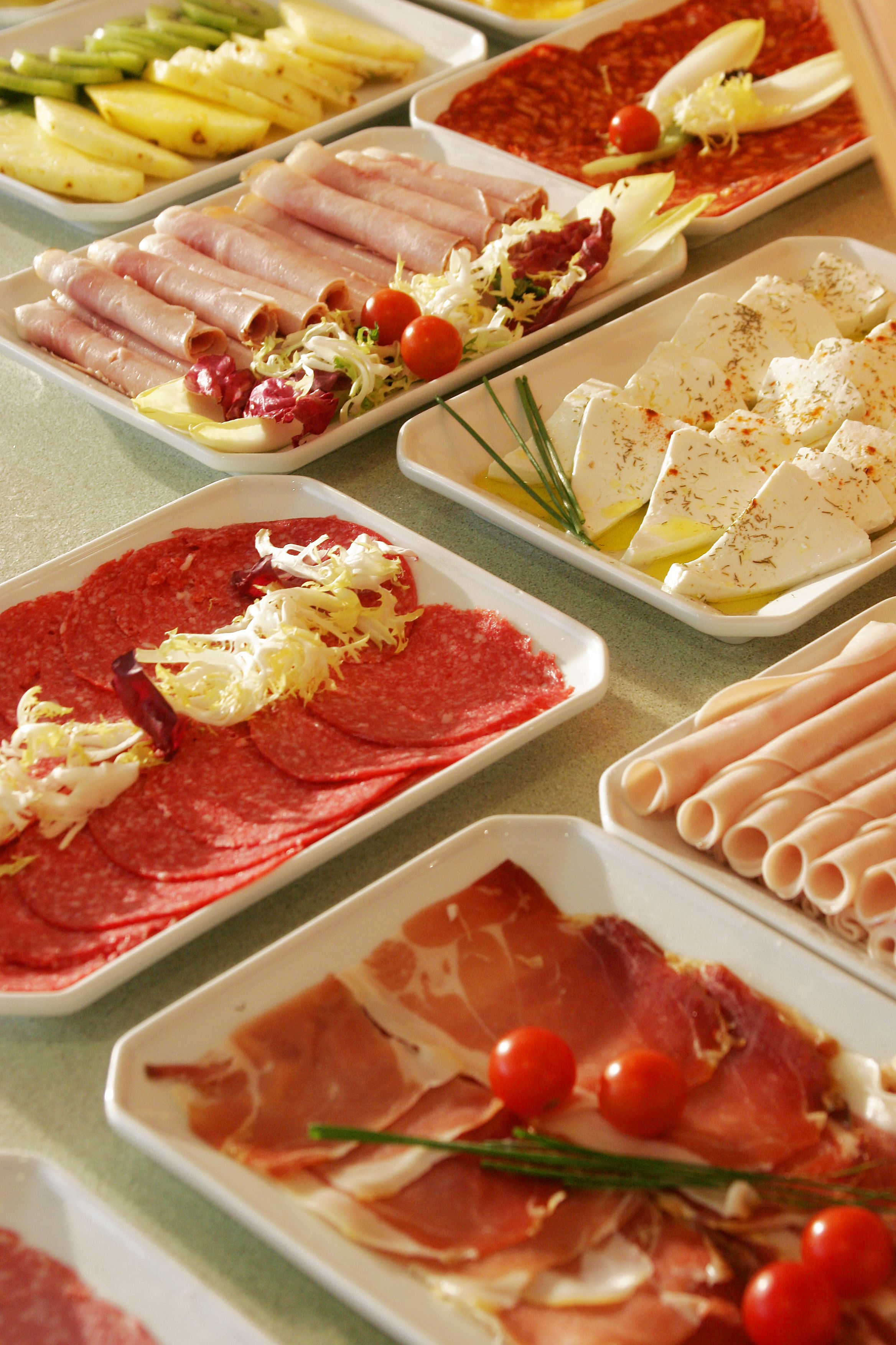 Diversos alimentos, incluindo carnes, queijos e vegetais, dispostos em pratos.