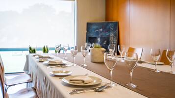 Uma mesa de jantar posta com pratos, copos e talheres, com vista para o exterior através de uma janela.