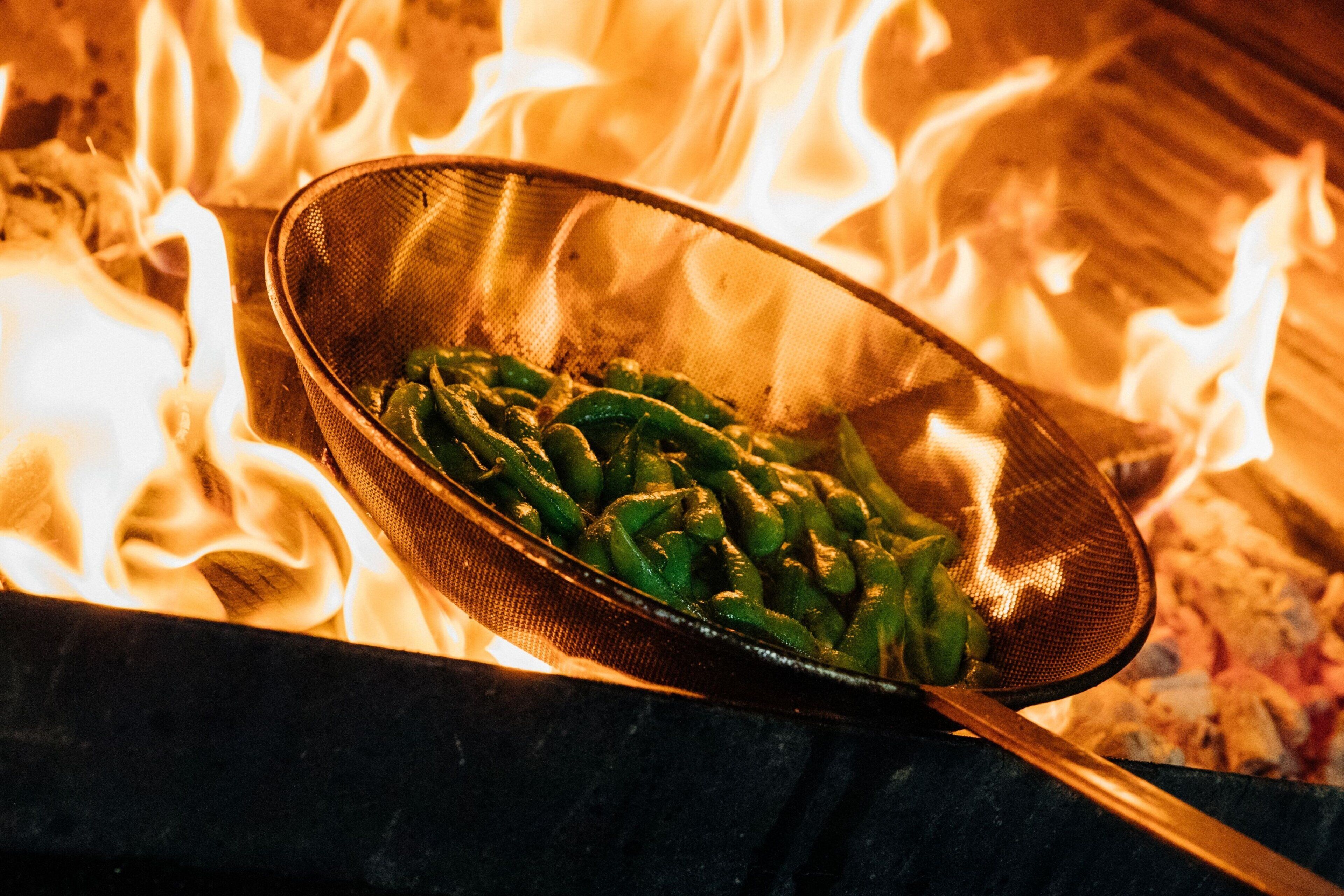 Uma peneira de metal com vegetais verdes sobre o fogo.
