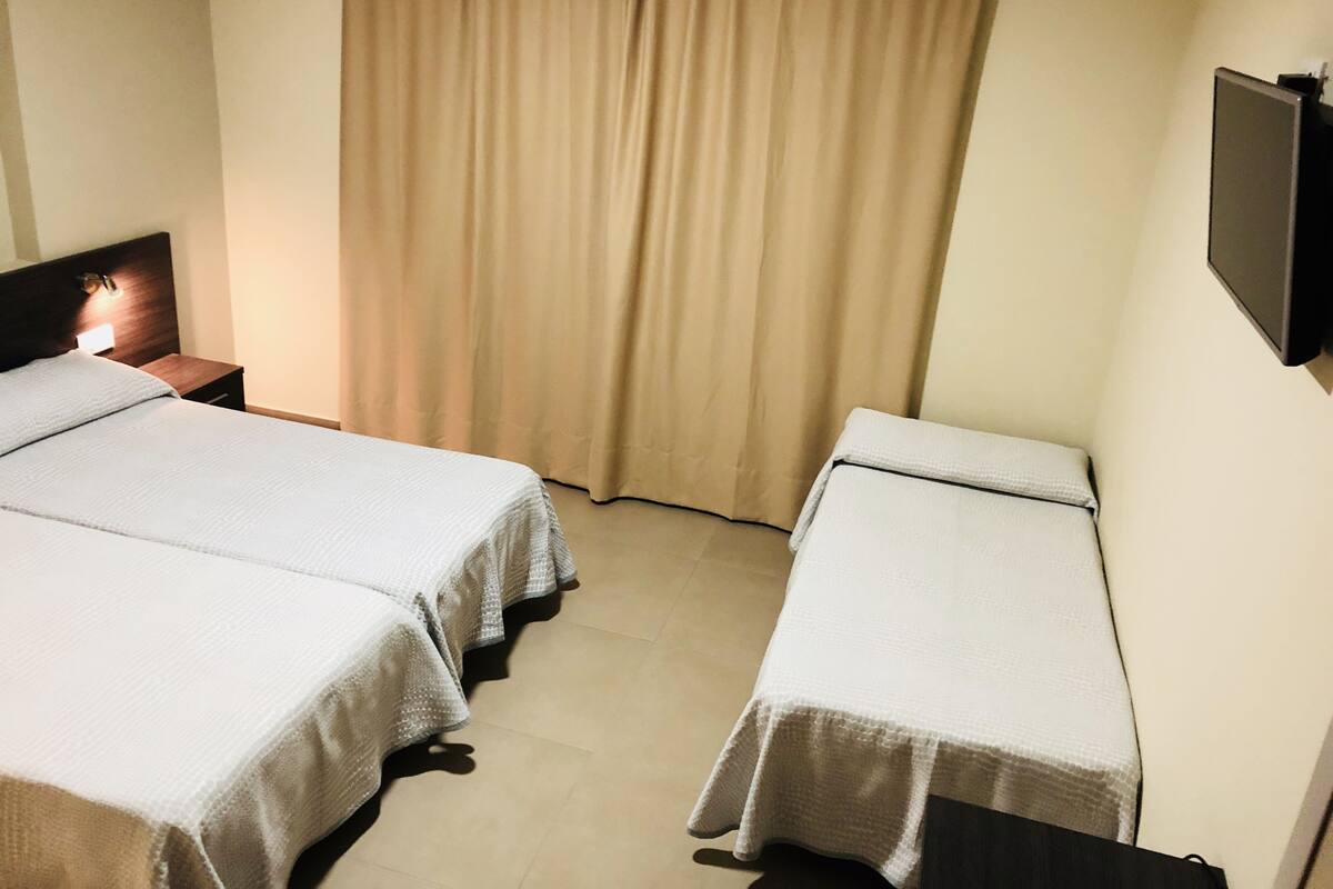 Quarto de hotel com duas camas, uma televisão na parede e uma cortina.