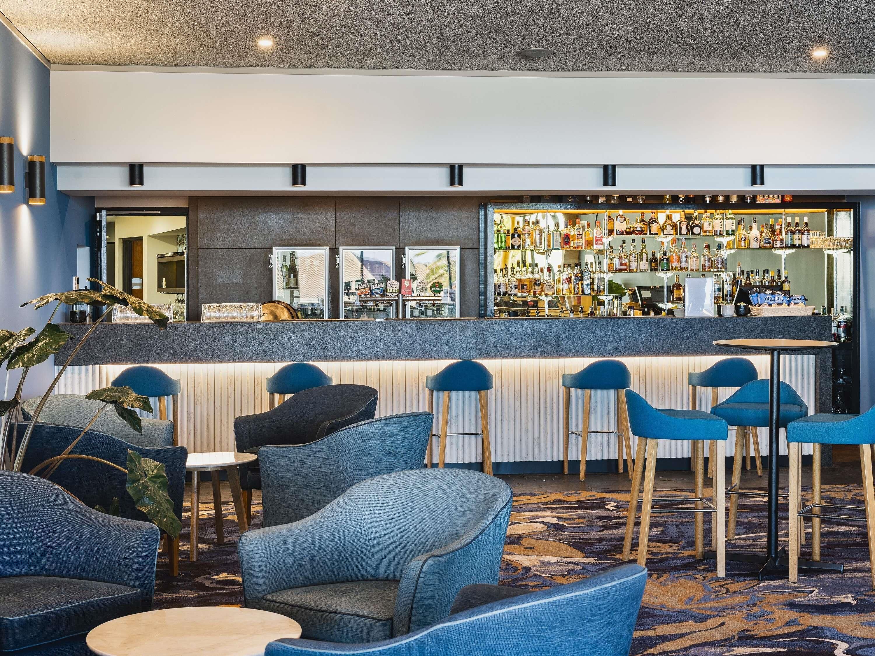 Uma área de bar com assentos, um balcão com diversos tipos de garrafas e vista para o bar.