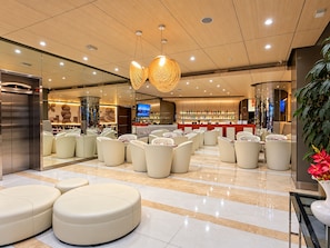 Um saguão moderno de hotel com assentos arredondados, área de bar e um espelho grande refletindo o espaço.