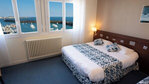 Quarto de hotel com uma cama grande, vista para o mar e uma janela com cortinas.