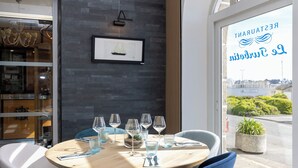 Um restaurante com uma mesa redonda posta para refeições, um quadro na parede e vista para a rua.