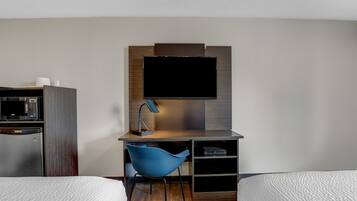 Quarto de hotel moderno com uma escrivaninha de madeira, uma cadeira azul, uma televisão de tela plana, um micro-ondas e um frigorífico.