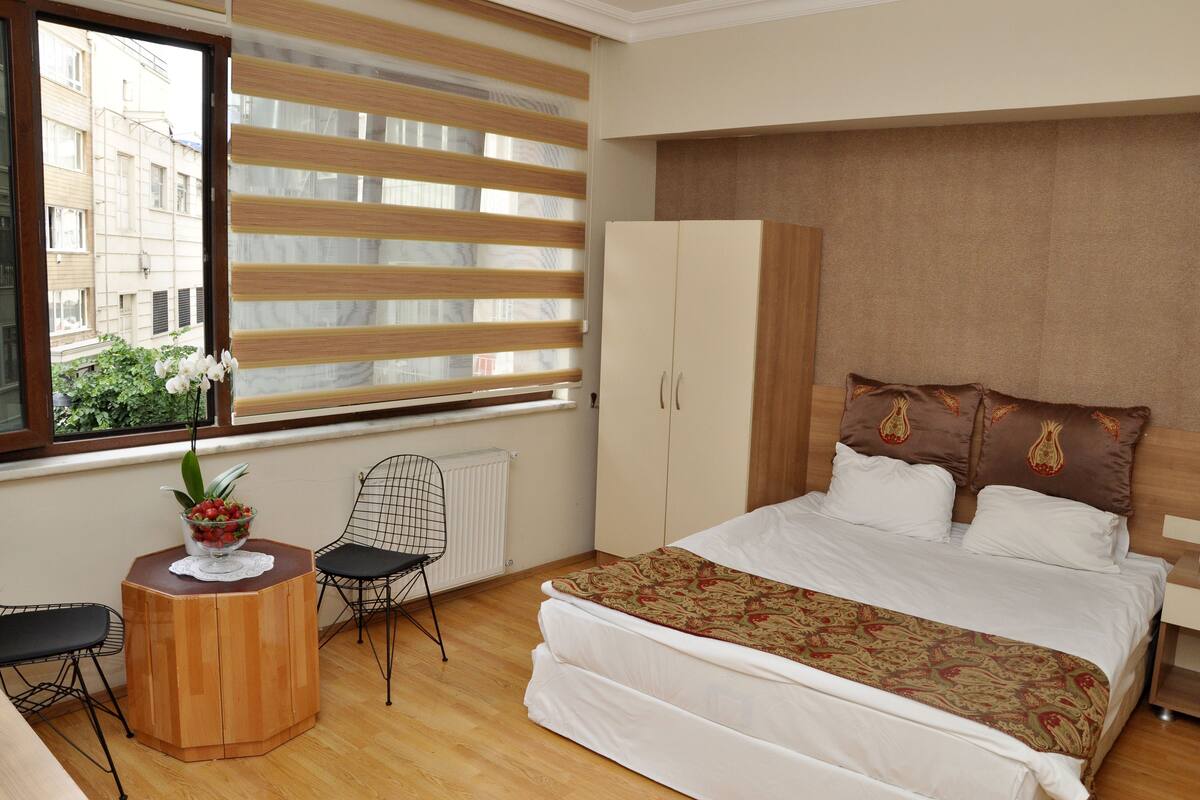 Quarto com cama, guarda-roupa, escrivaninha com cadeira e janela com persianas.