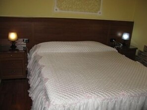 Uma cama bem arrumada com edredom branco, cabeceira de madeira e mesa de cabeceira com abajur.