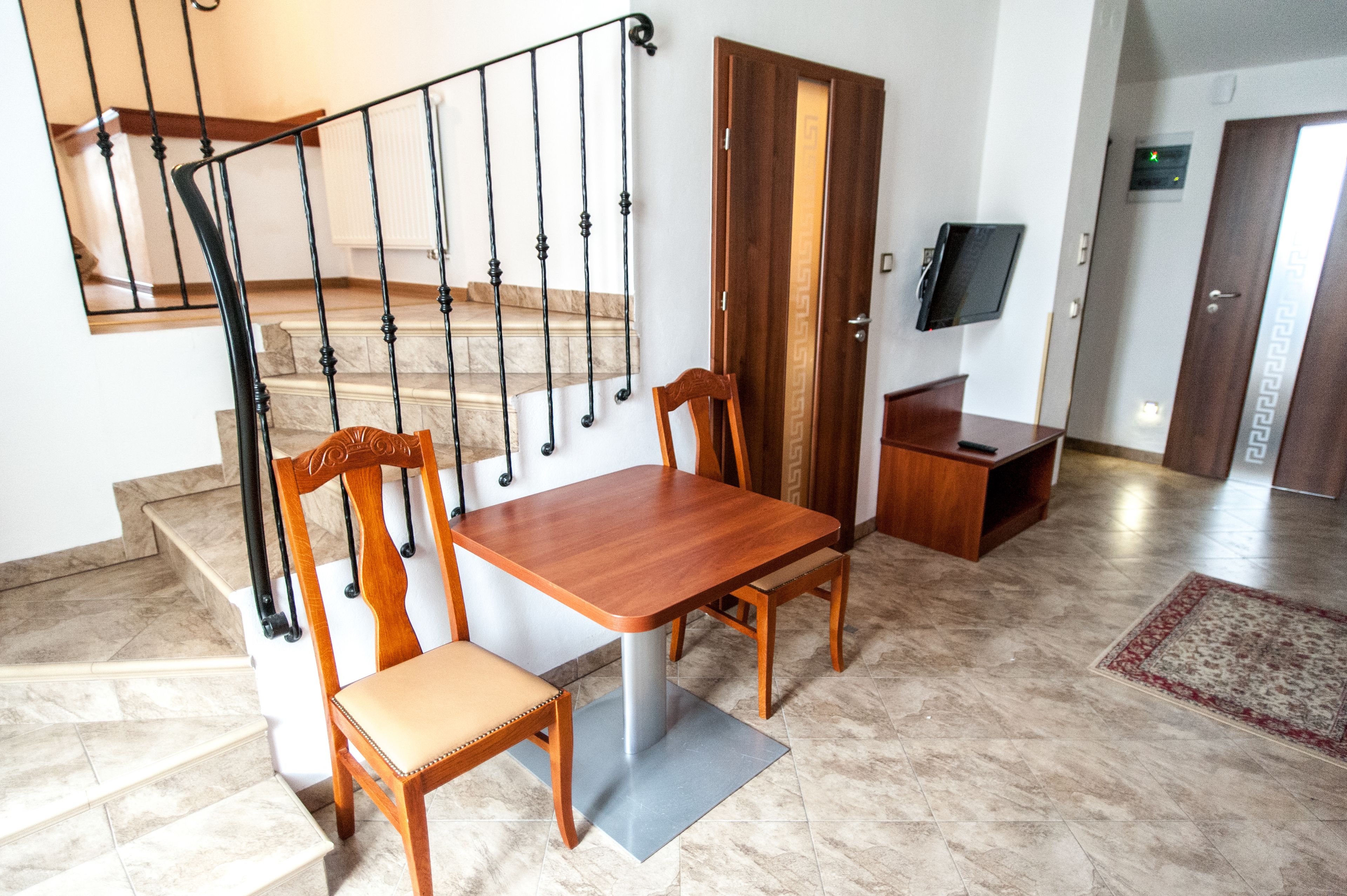 Uma sala de jantar com mesa e cadeiras de madeira, escada com corrimão de metal e porta de madeira com espelho.