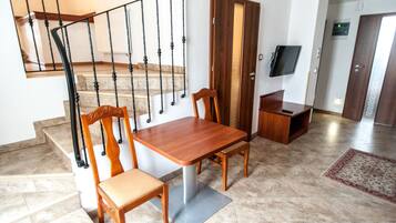 Uma sala de jantar com mesa e cadeiras de madeira, escada com corrimão de metal e porta de madeira com espelho.