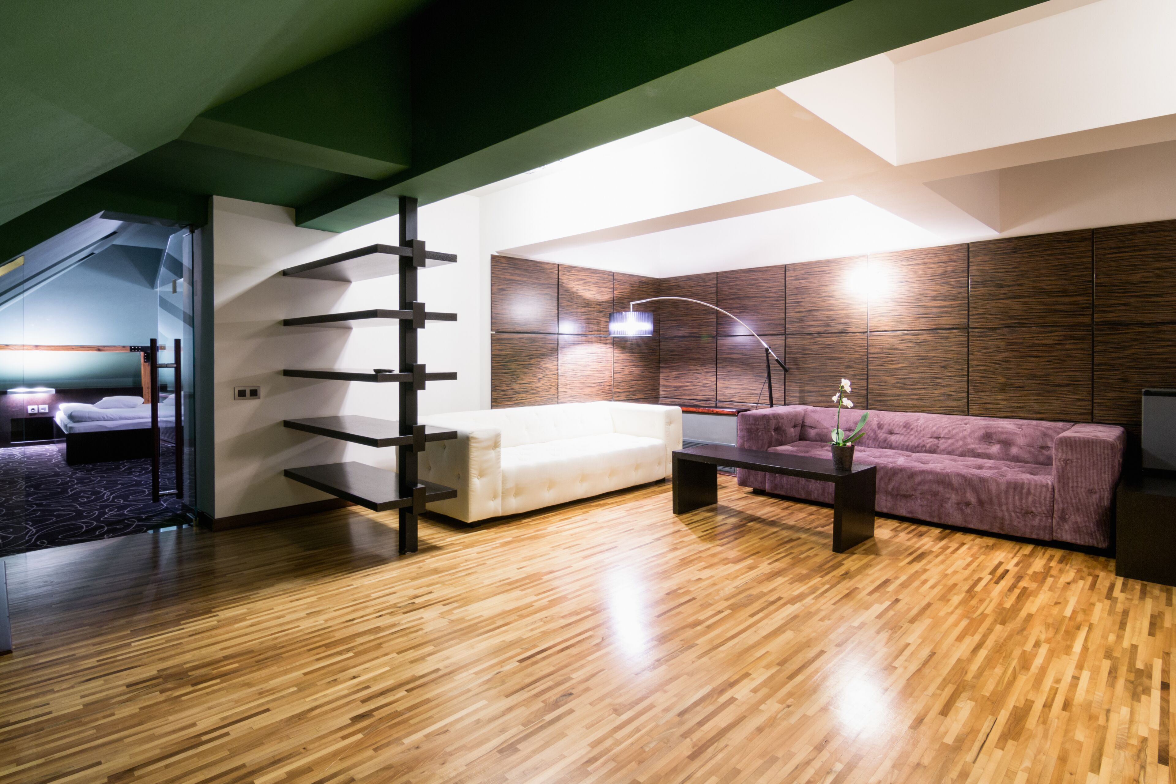 Uma sala de estar moderna com piso de madeira, um sofá branco, um sofá roxo, uma mesa de centro preta e uma televisão.