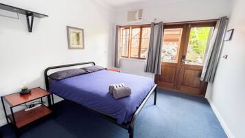 Quarto com cama, mesa de cabeceira, janela com cortinas e porta que dá para o exterior.