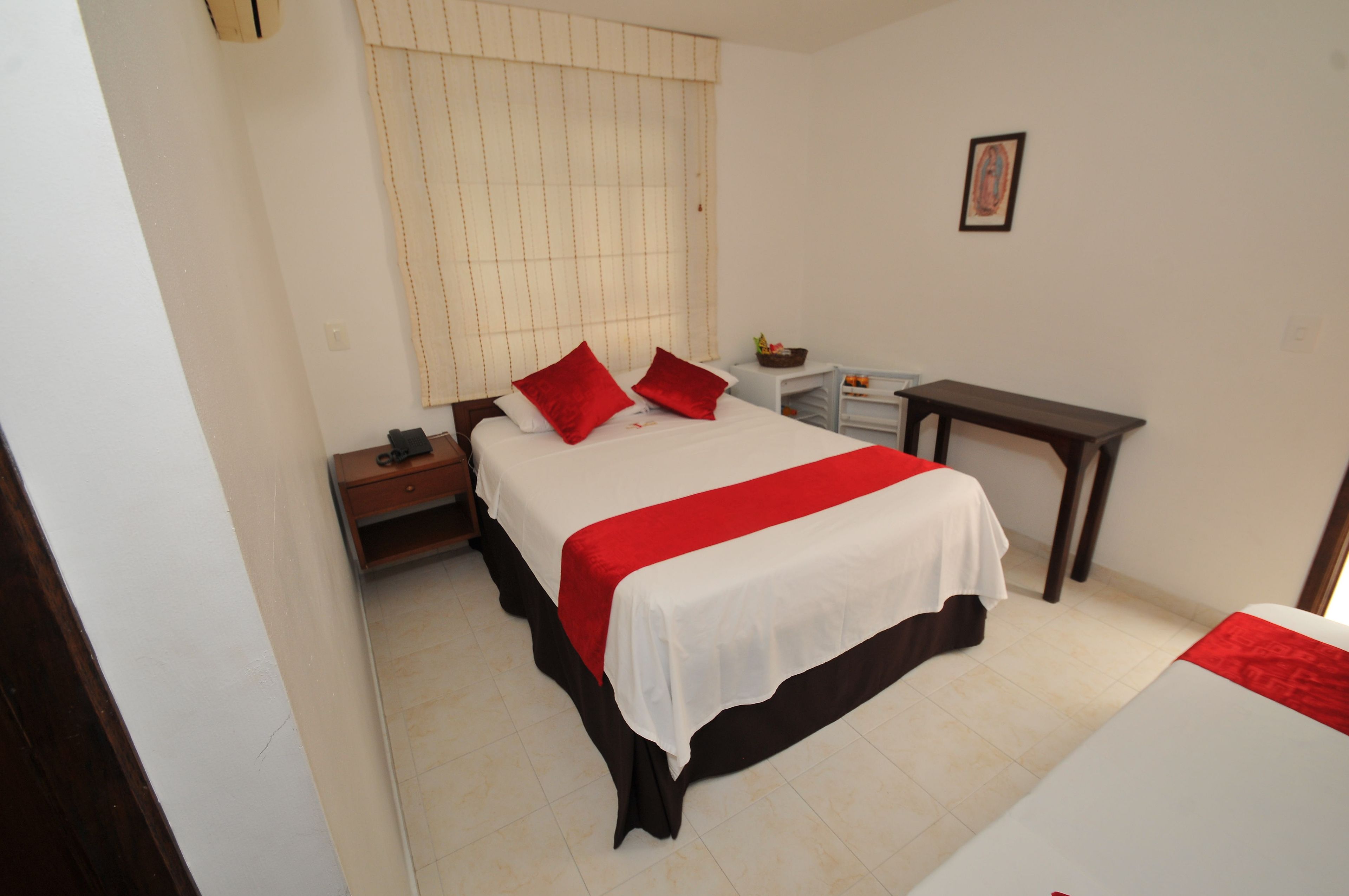 Quarto bem arrumado com cama, mesa de cabeceira e escrivaninha.