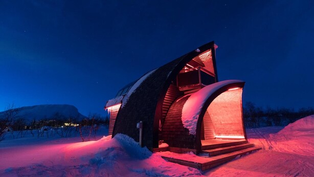 Um edifício moderno com arquitetura em arco e luz interior acolhedora, rodeado por neve.
