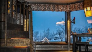 Um interior moderno com escadas, área de refeições e uma grande janela com vista para uma paisagem coberta de neve.
